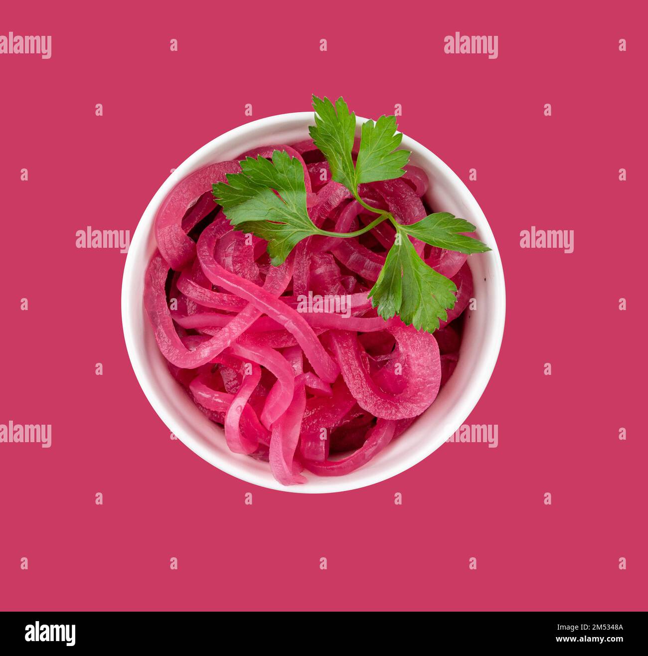Pickled red onion rings in a white bowl with fresh herbs on magenta ...