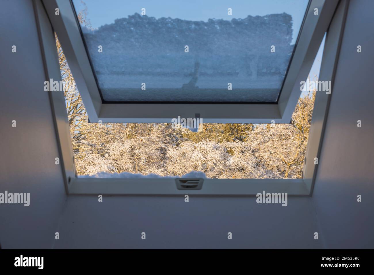 View from snow covered dormer window on roof of house to forest trees ...