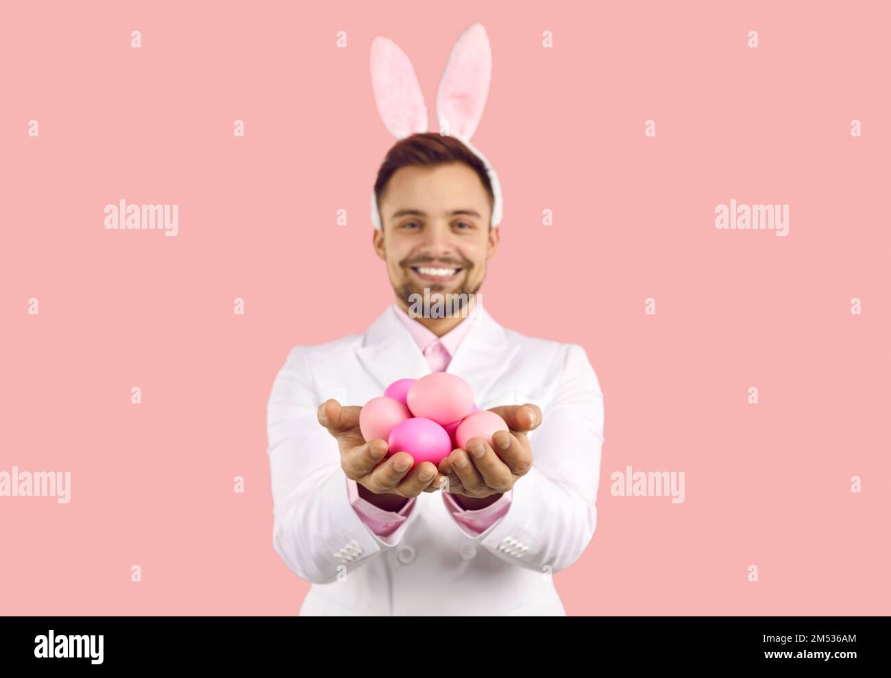 Smiling man wearing bunny ears holding Easter eggs isolated on pastel ...