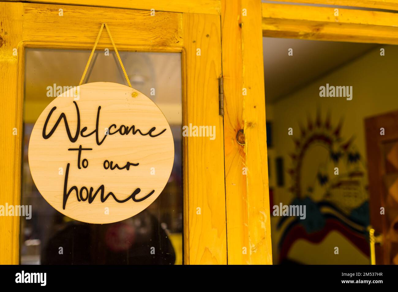 A closeup of a round wooden sign saying "welcome to our home" in front ...