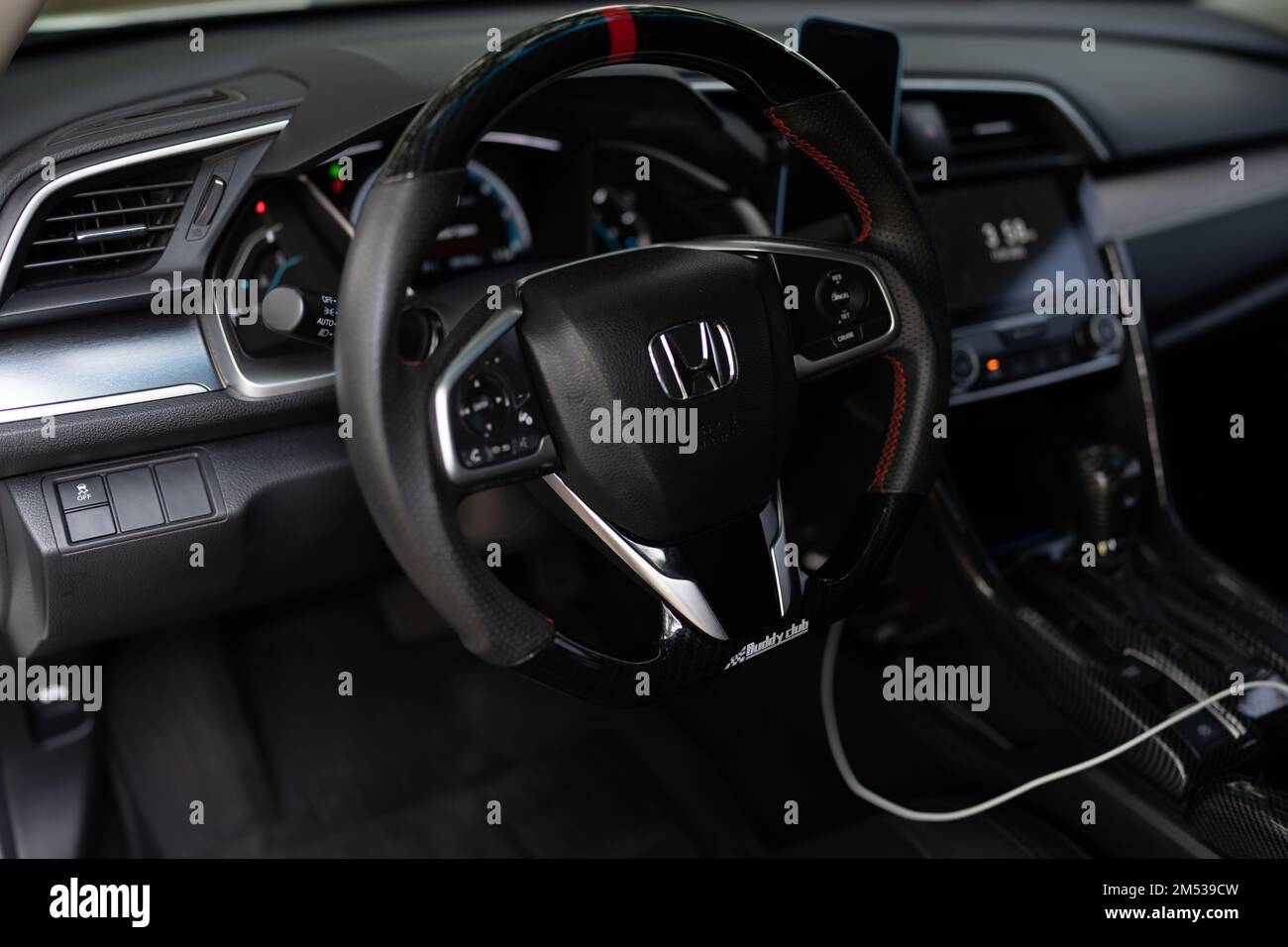 A closeup of the black steering wheel with red lines and the silver ...