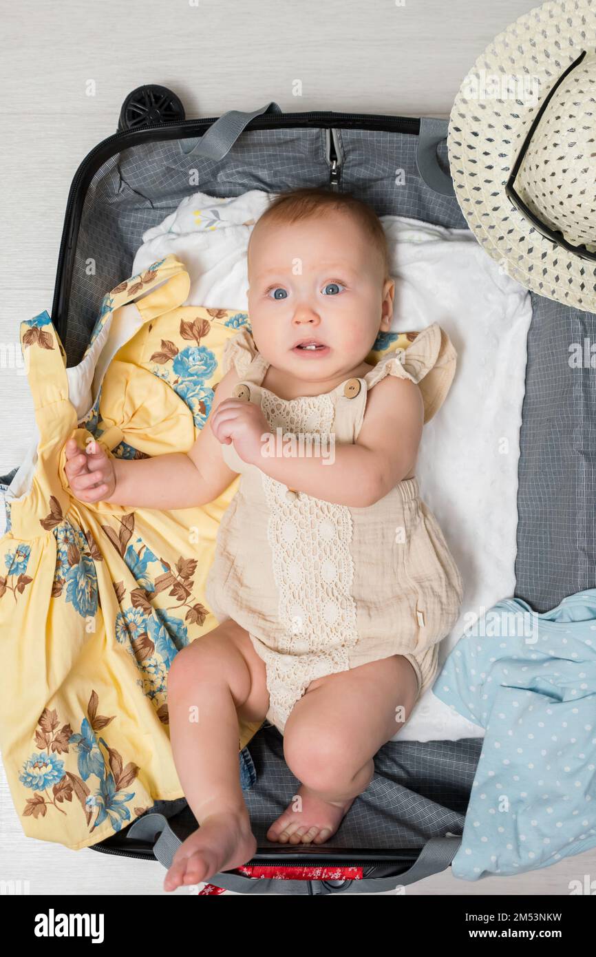 Baby girl with excited and amused expression lies in suitcase with ...