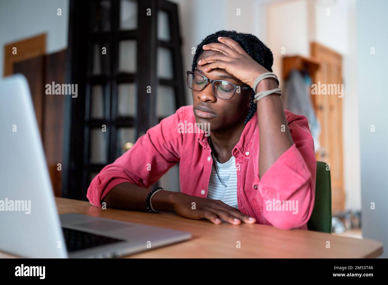 Oppressed sad African American man closed eyes sits at table with ...
