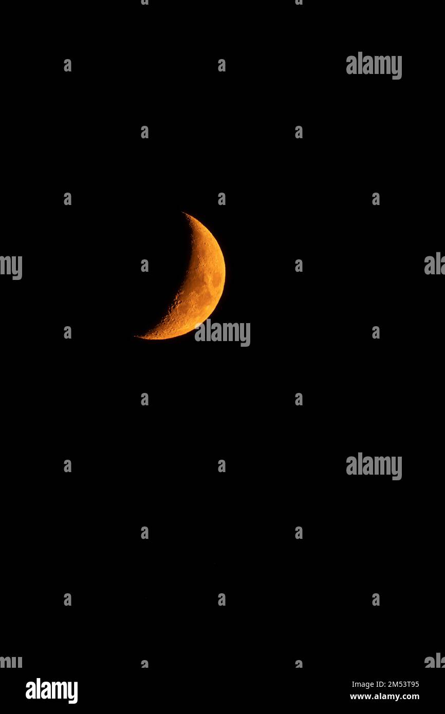 A vertical shot of the orange spooky crescent of the moon in the black ...