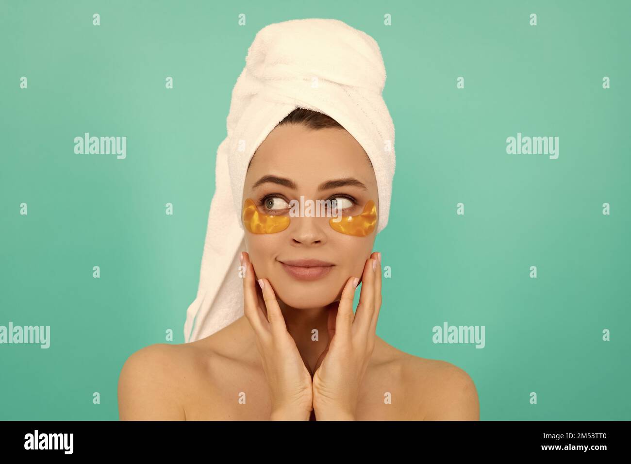 smiling young lady has collagen golden eye patches on face with towel ...