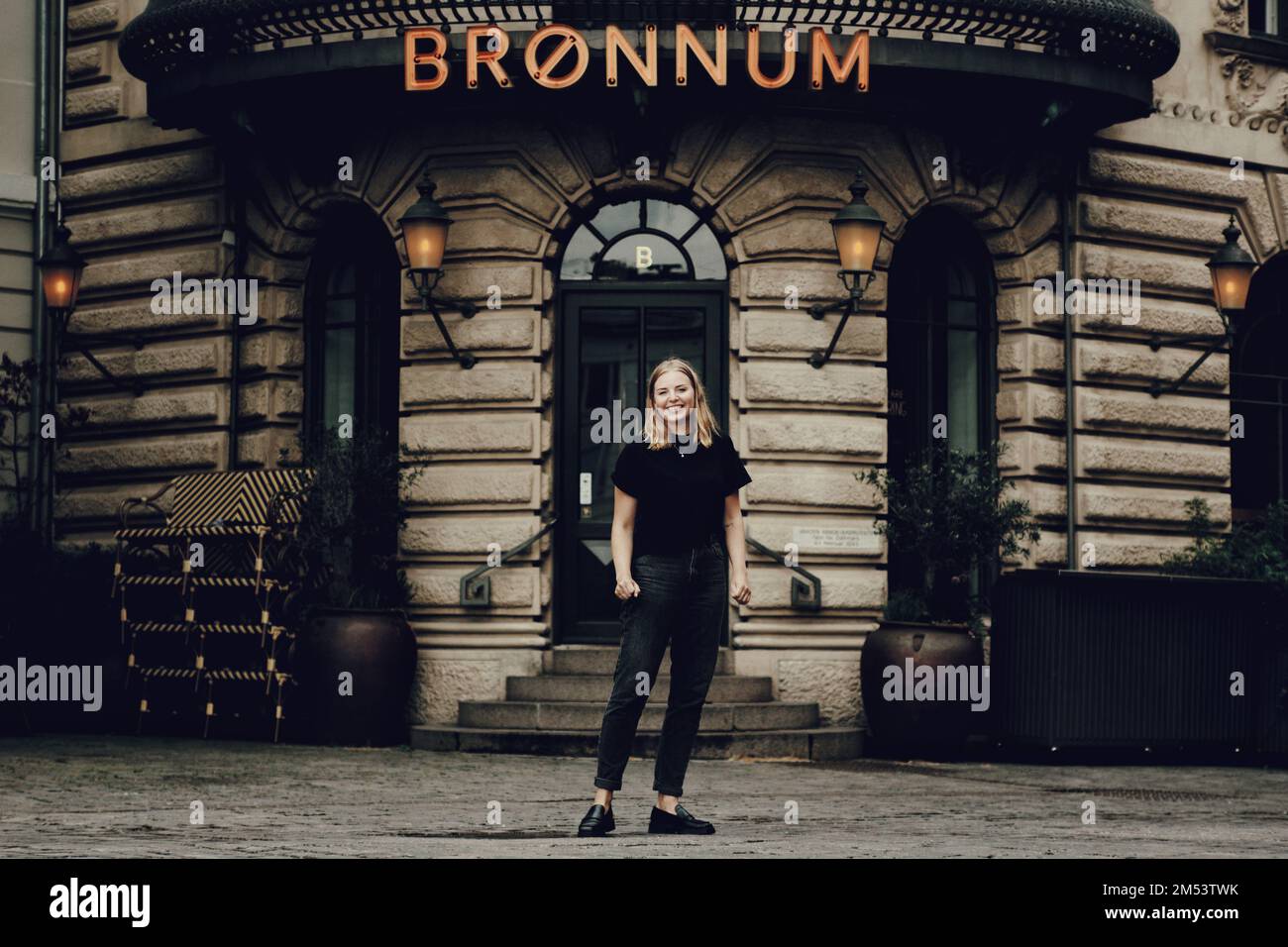 A smiling female journalist in black standing in front of a bar in ...