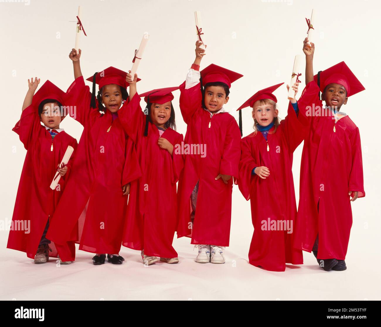 Group of children in red graduation gowns and mortar boards holding ...