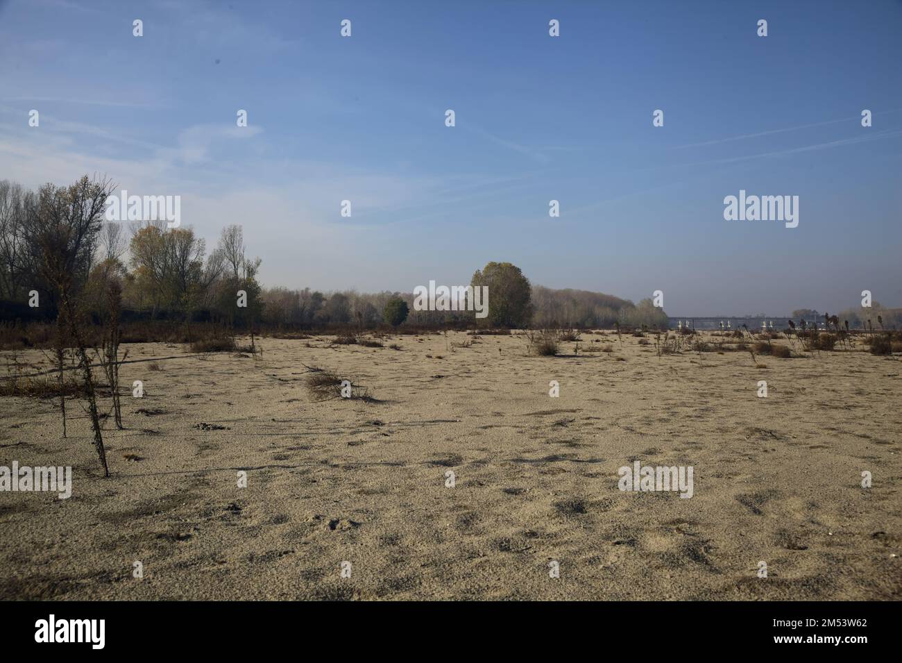 Sandy rivershore dotted by bushes with a bridge over the river on the ...