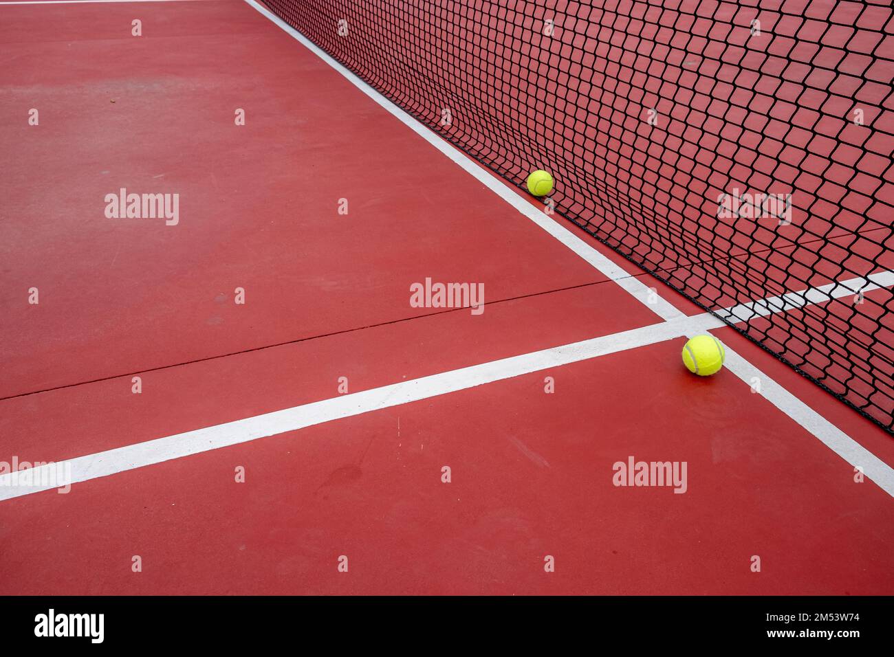 The two tennis balls resting by the net and court lines on a red ...