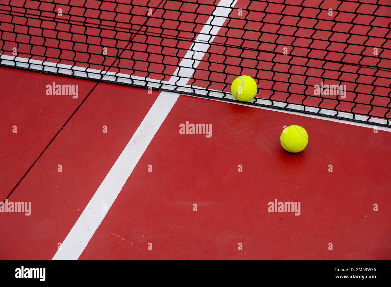 The two tennis balls resting by the net and court lines on a red ...