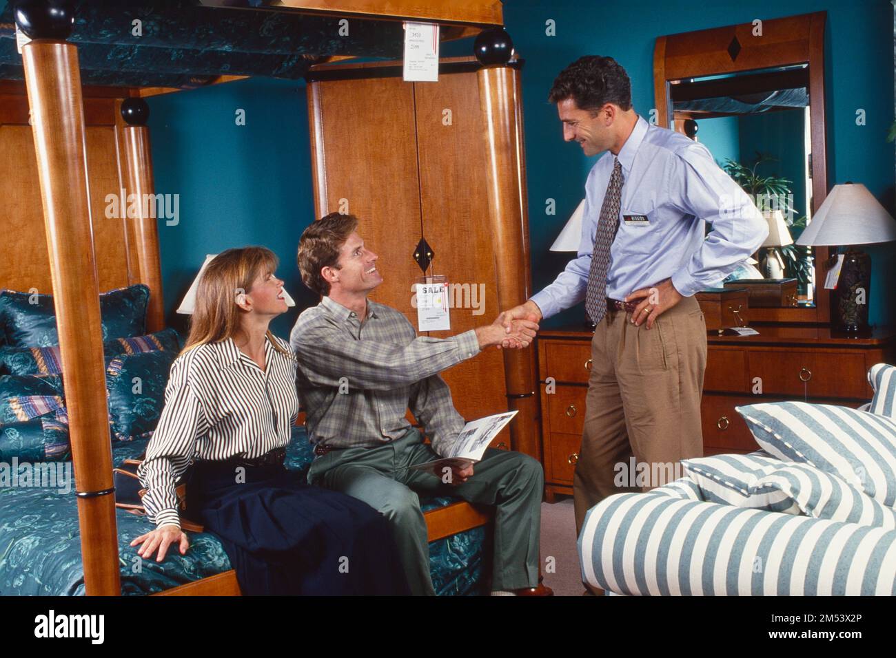 Young couple in a furniture store with salesman shaking hands. After ...