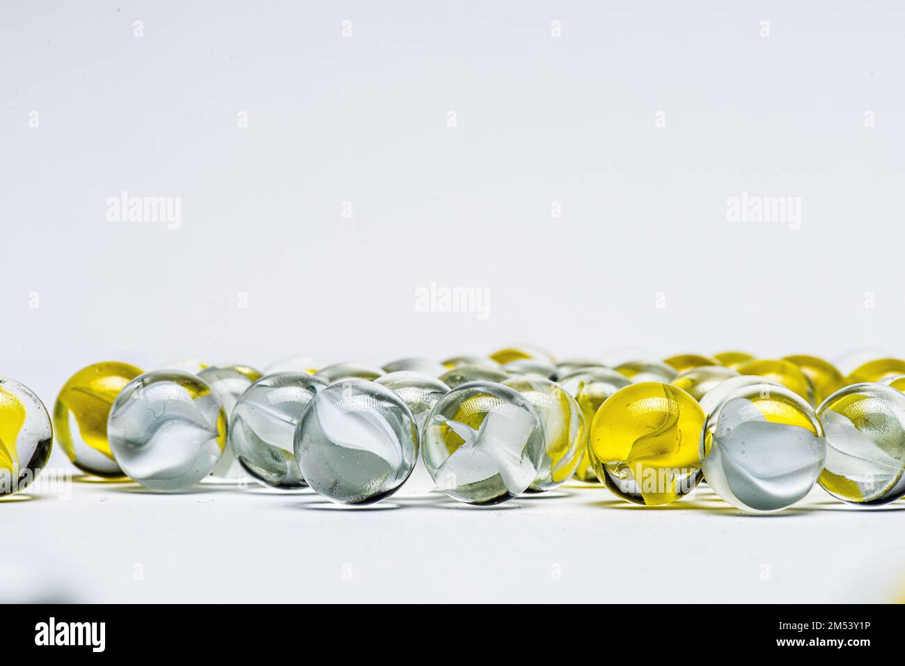 A closeup of a pile of Yellow and white glass marbles isolated on white ...