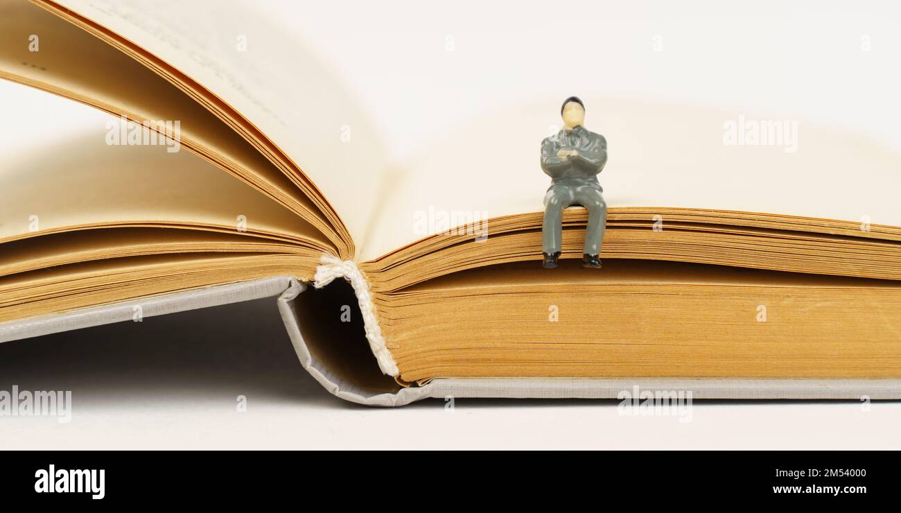 Education concept. A miniature human figure sits on the pages of an ...