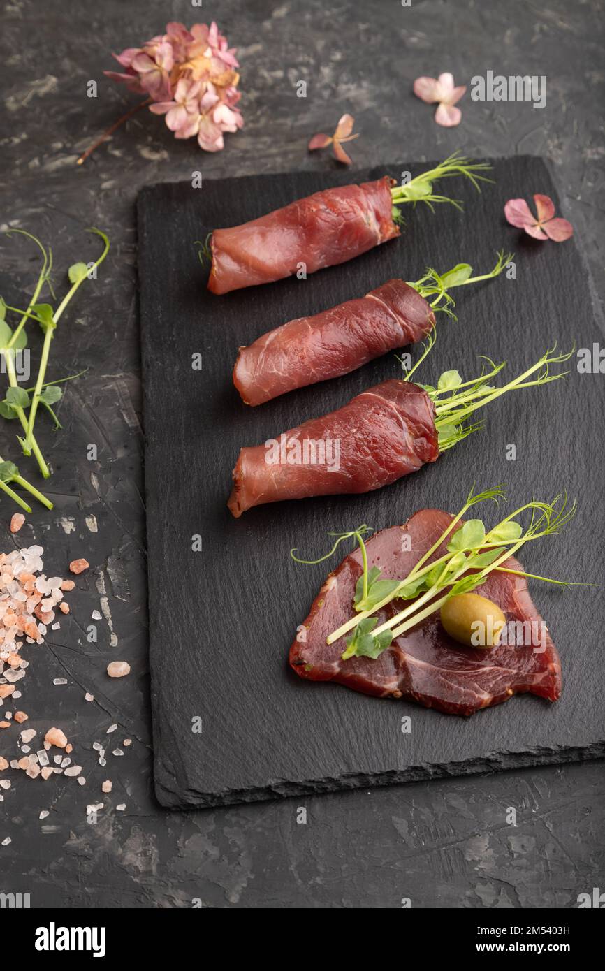Slices of smoked salted meat with green pea microgreen on black ...