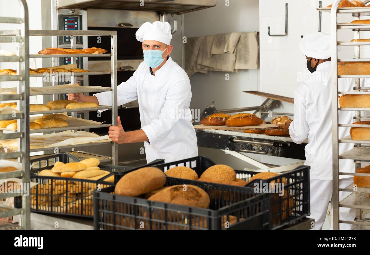 Man in protective mask transporting cart with bread in bakery Stock ...