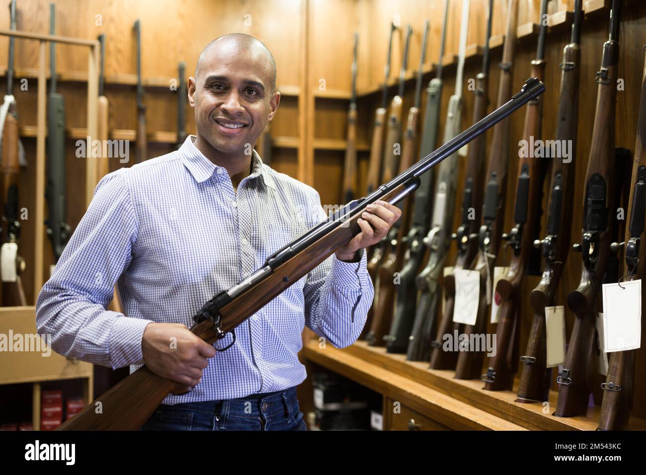 Happy hispanic man standing with hunting rifle at gun shop Stock Photo ...