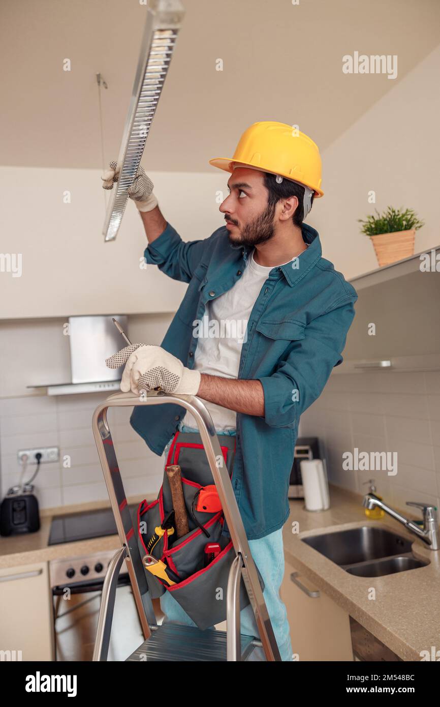 Professional electrician worker in uniform is installing electric lamps ...