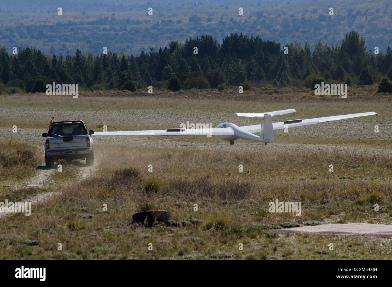 A ultralight glider plane landing with van waiting to tow it with trees ...