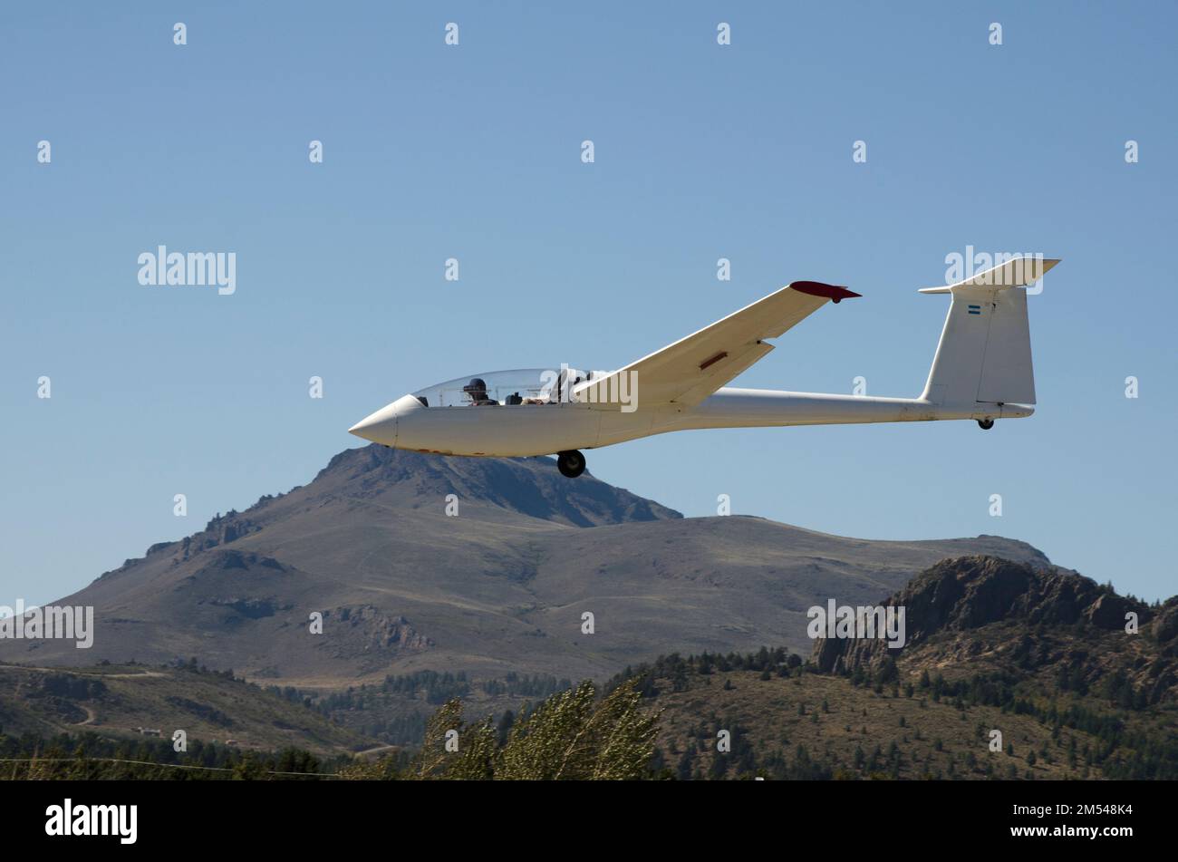 An ultralight glider plane flying near mountains, landing on earth ...
