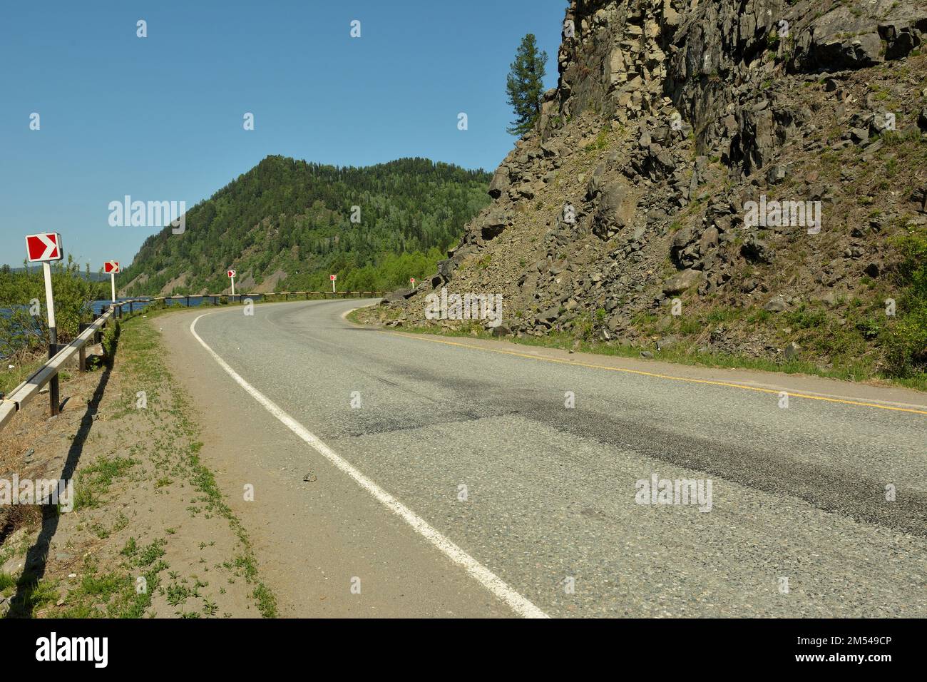 Right turn of an asphalt road with fences at the foot of high mountains ...