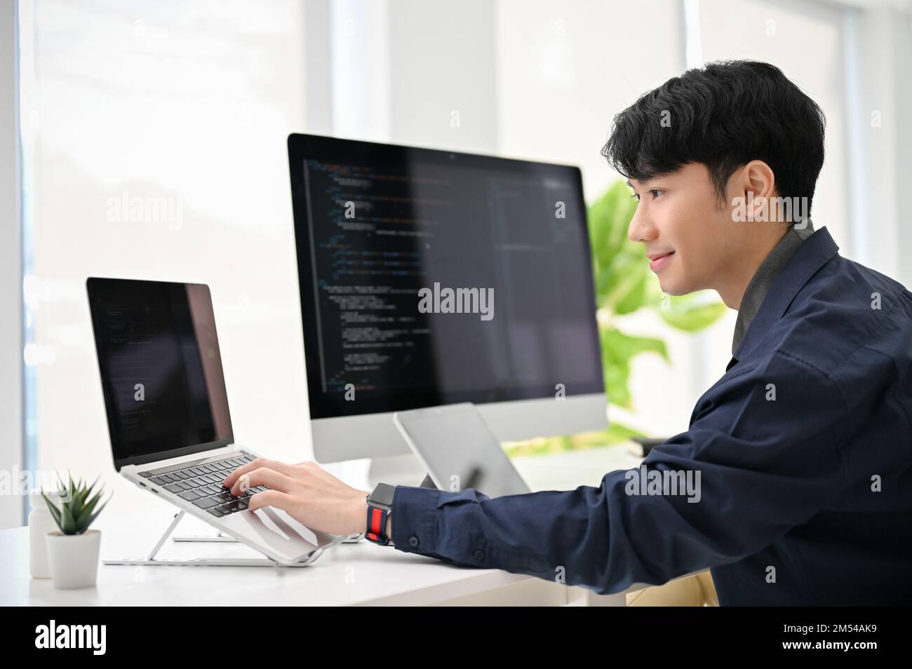 Professional and smart young Asian male programmer coding at his desk, working on his project ...