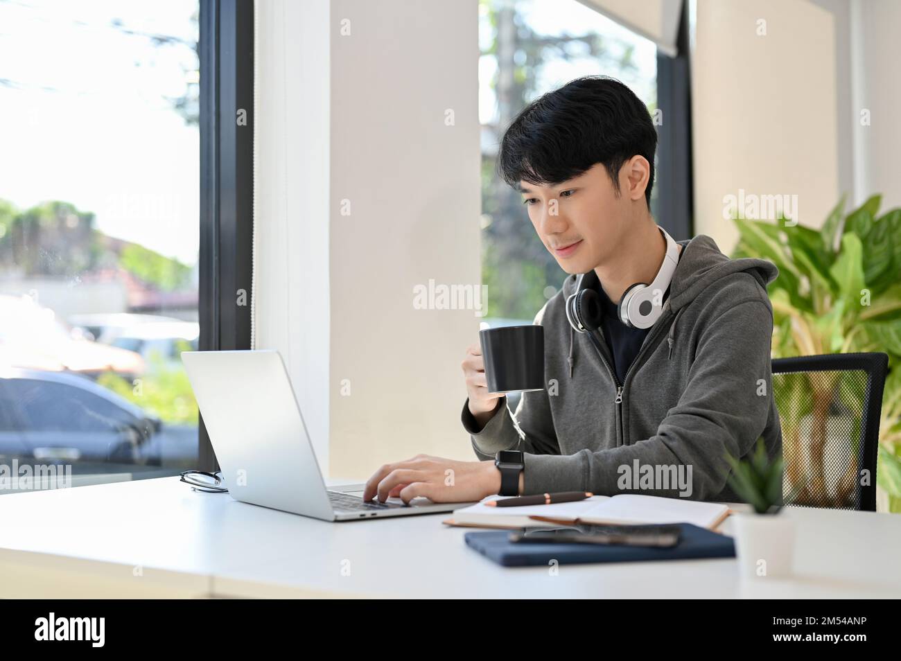 Smart young Asian male programmer or web developer sipping morning ...