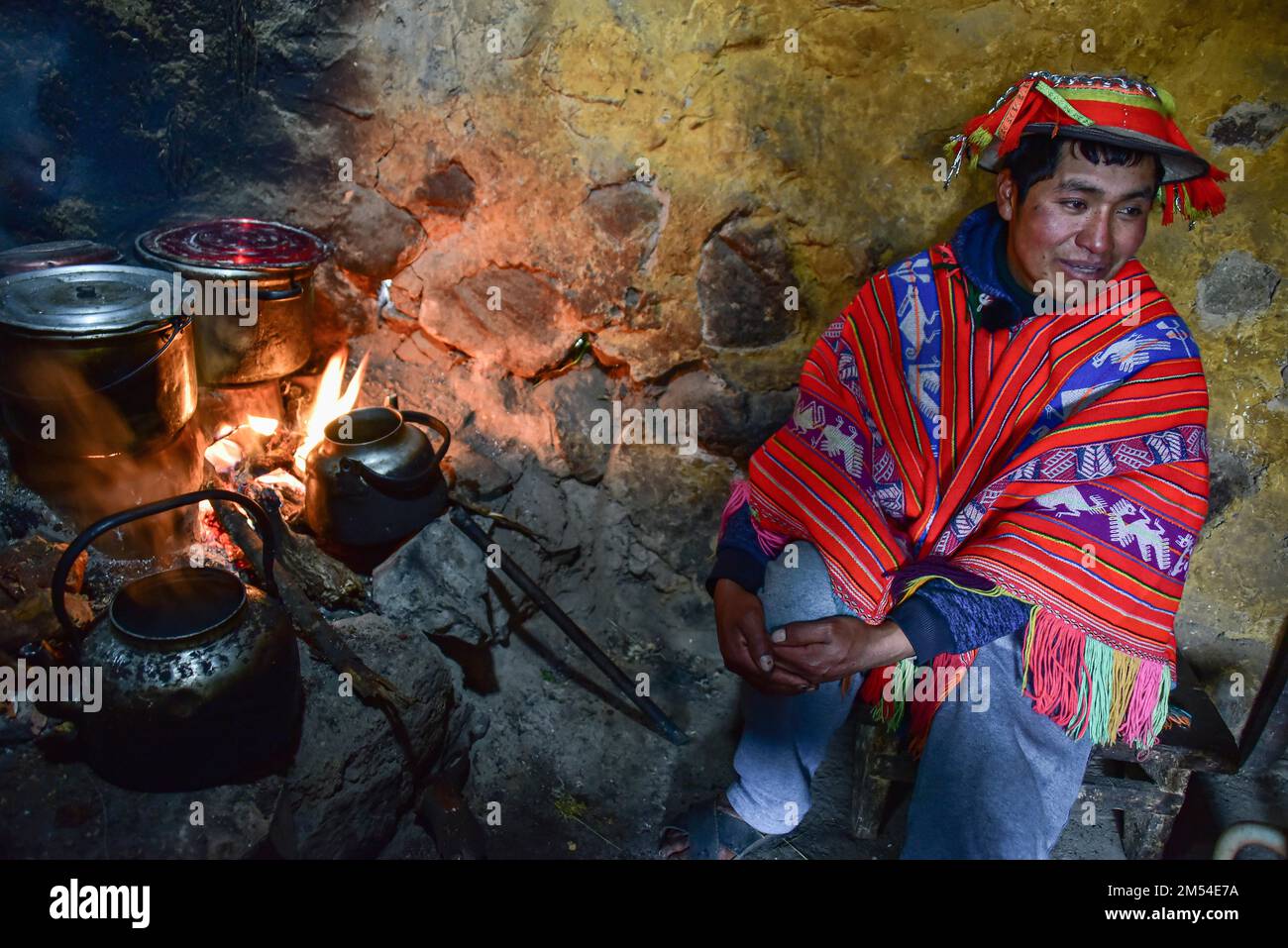 Quechua Indian in traditional dress cooking at the fireplace of his hut ...