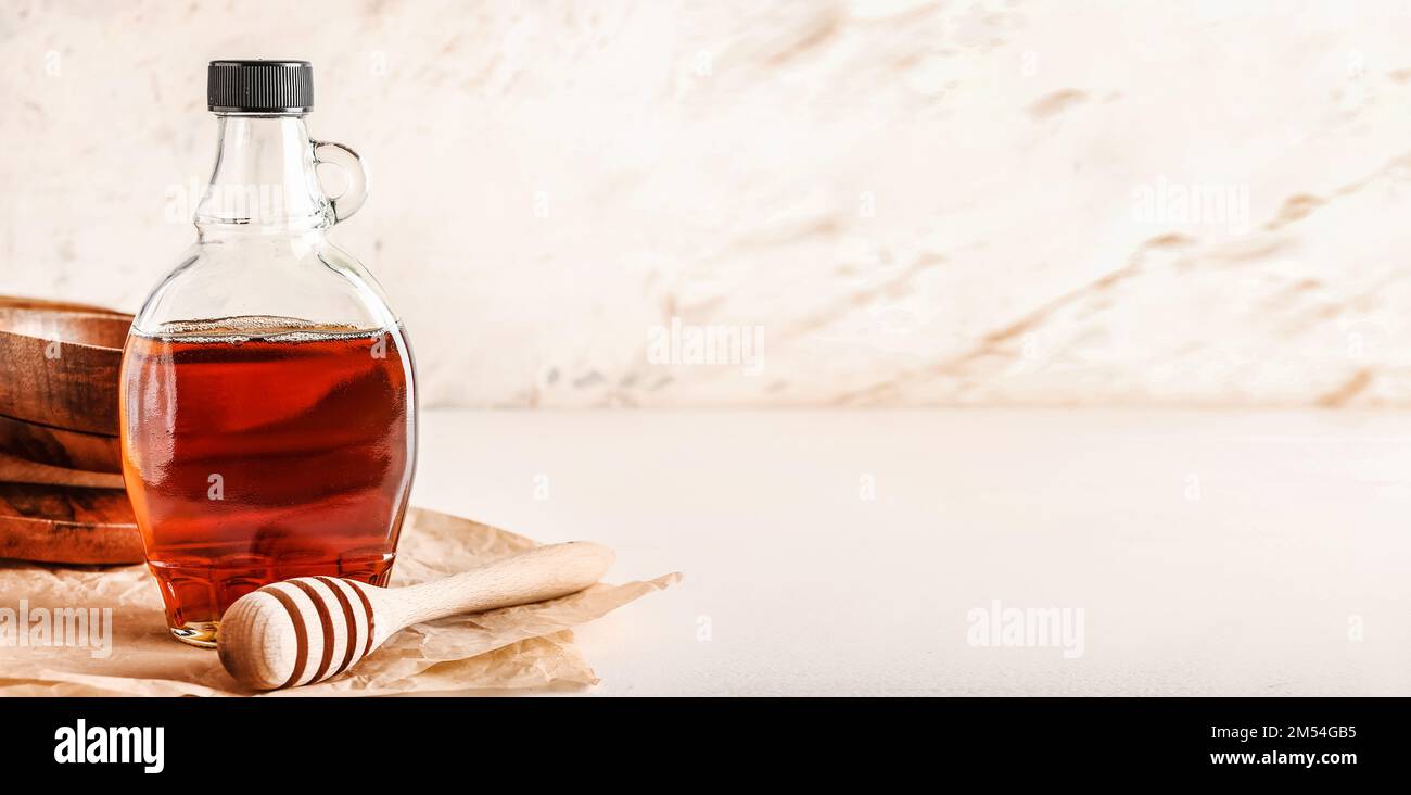Bottle of tasty maple syrup and honey dipper on light background with ...