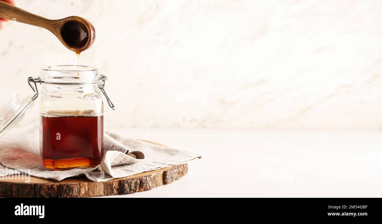 Pouring of maple syrup from spoon into jar on light background with ...