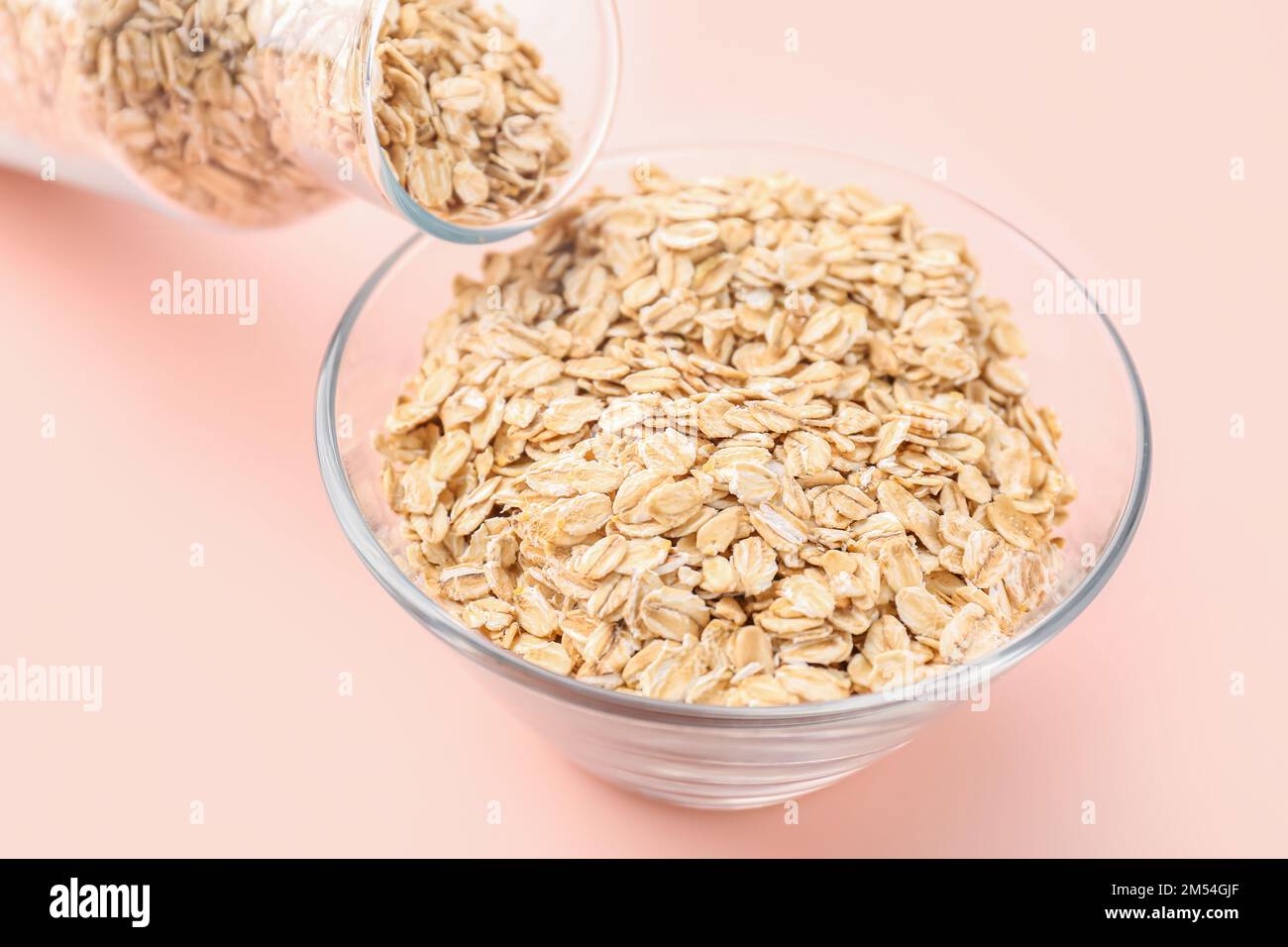 Pouring of raw oatmeal from bottle into bowl on pink background ...