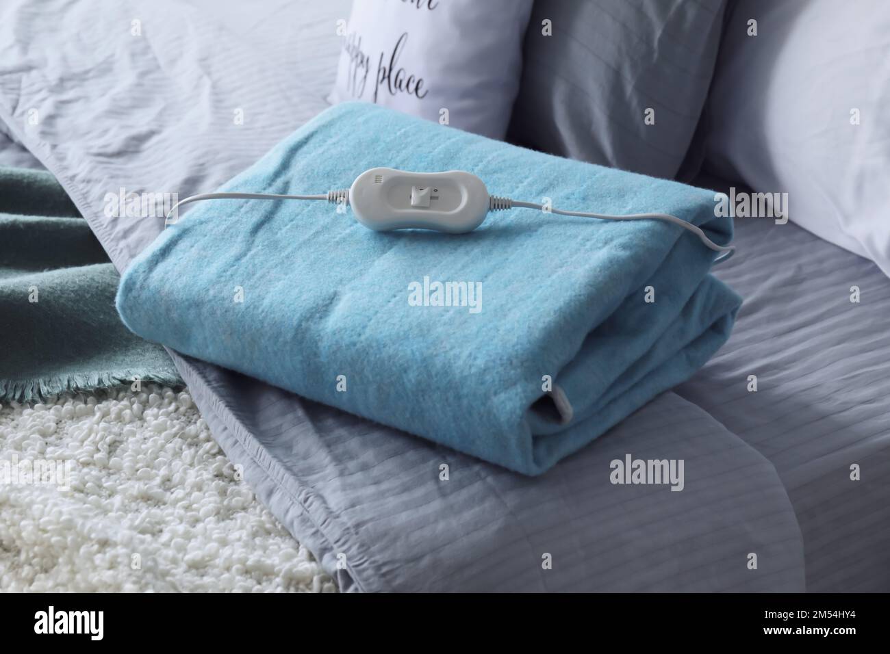 Folded electric heating pad with controller on bed in bedroom, closeup ...