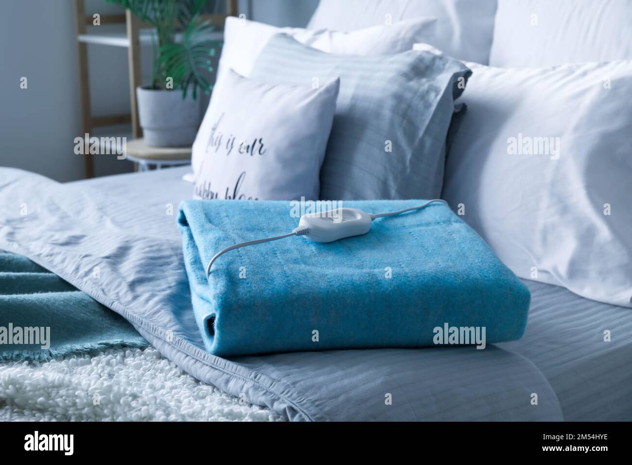Folded electric heating pad with controller on bed in bedroom, closeup ...
