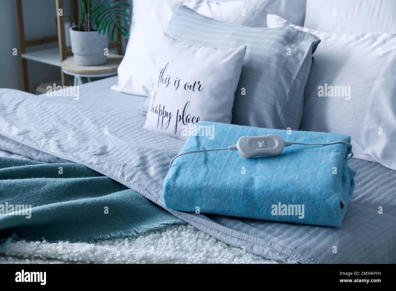Folded electric heating pad with controller on bed in bedroom, closeup ...