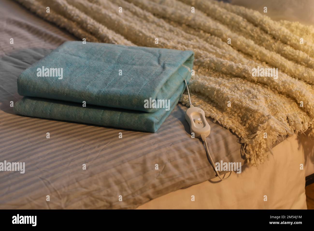 Folded electric heating pad with controller on bed in dark room ...