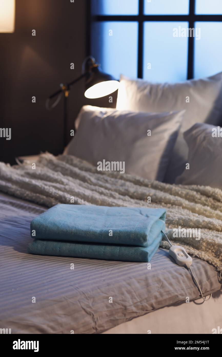 Folded electric heating pad with controller on bed in dark room ...