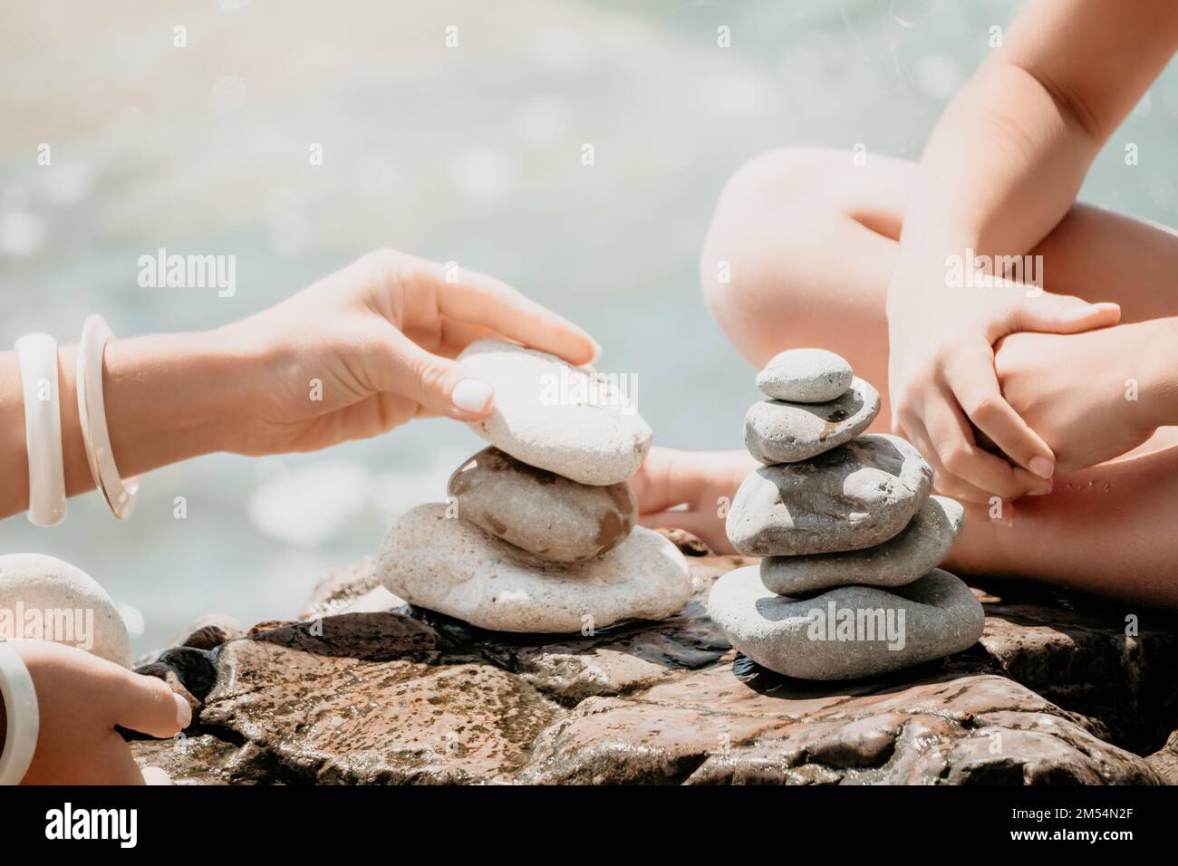 Woman with daughter bilds stones pyramid on seashore on a sunny day on ...