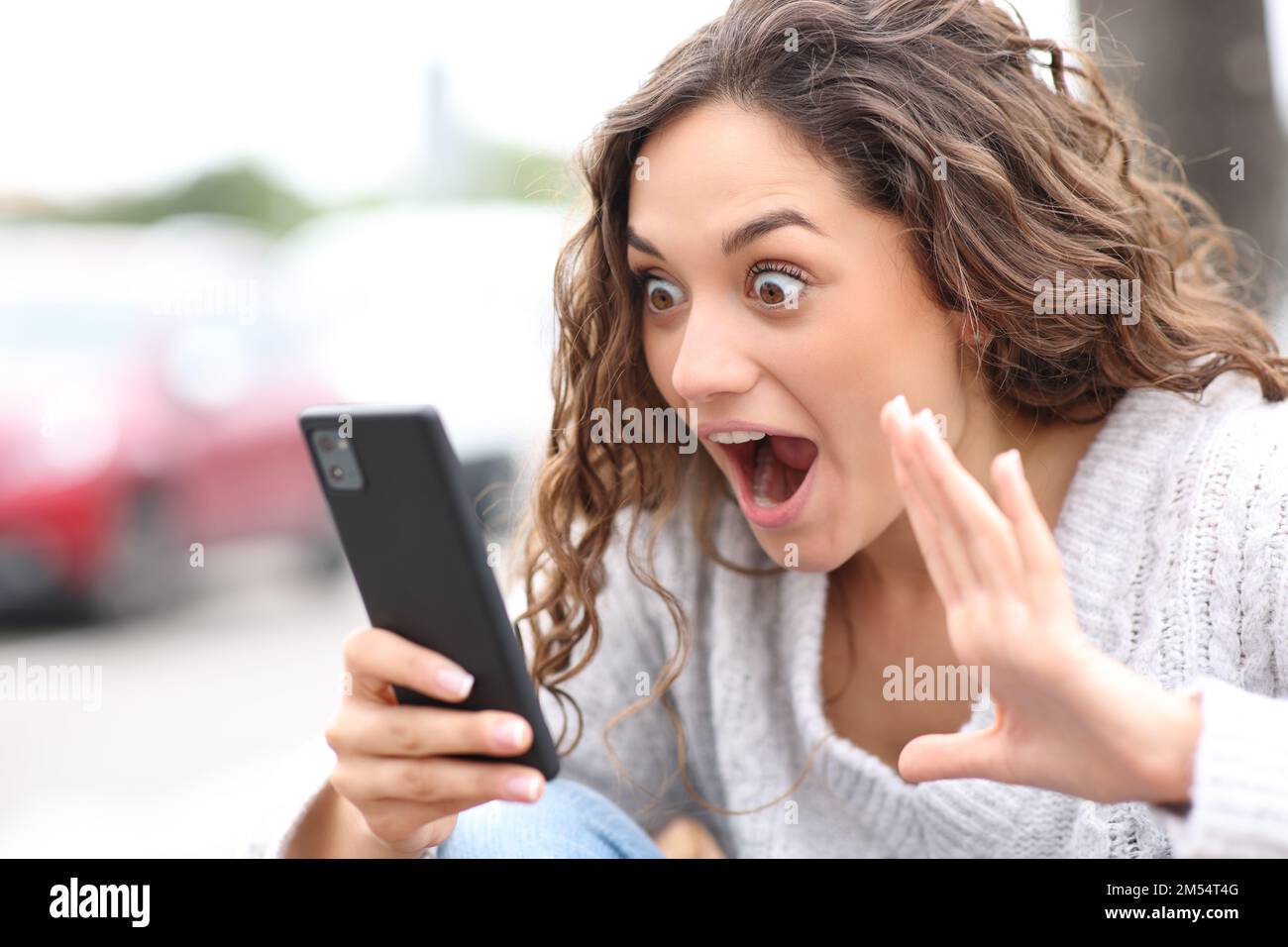 Surprised woman checking smart phone content in the street Stock Photo - Alamy