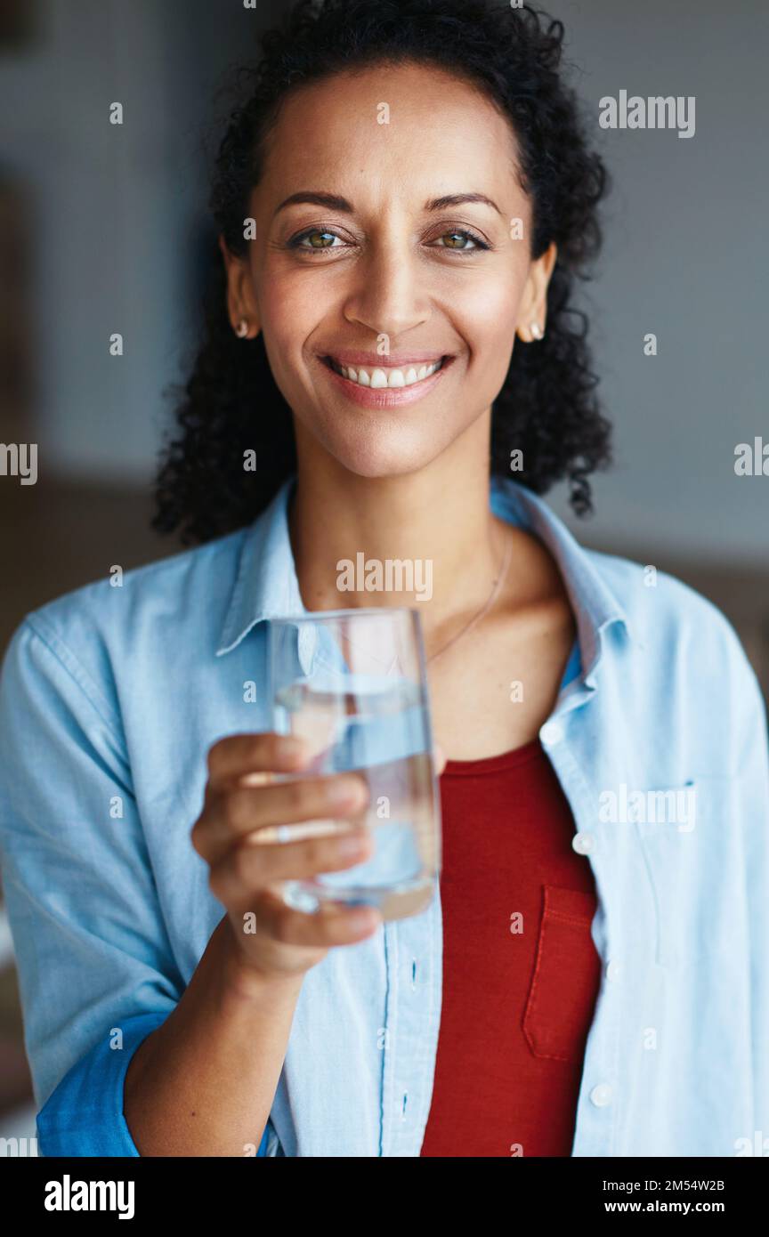 Remember to drink your eight glasses daily. Portrait of a woman drinking a glass of water at ...