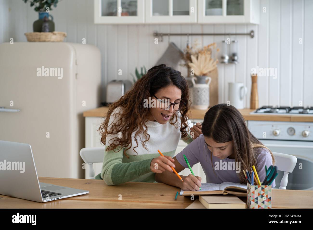 Young mother helping schoolgirl daughter to do homework, juggling kids ...