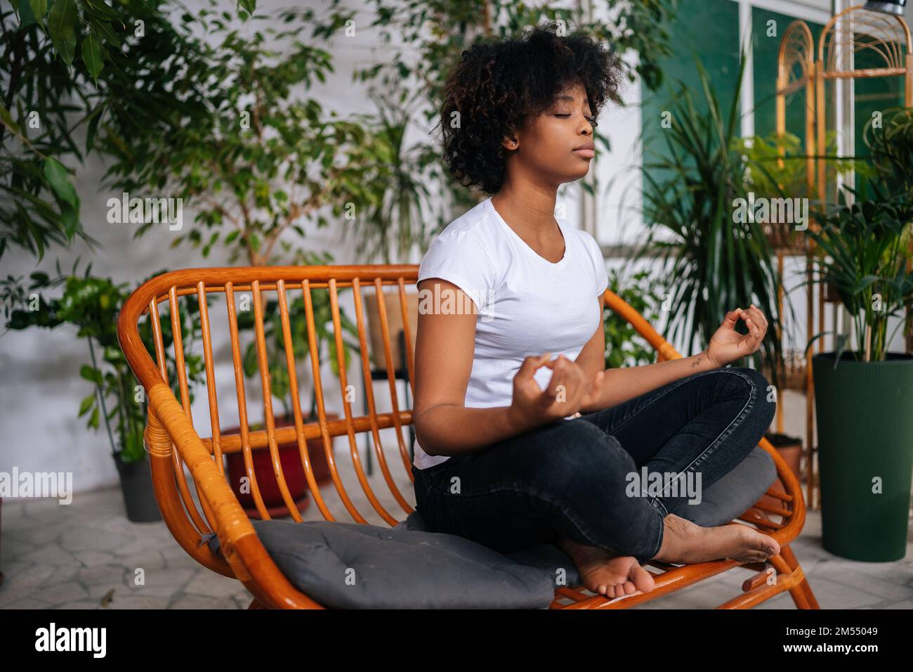 Mindful barefoot black young woman sitting with closed eyes on sofa in ...