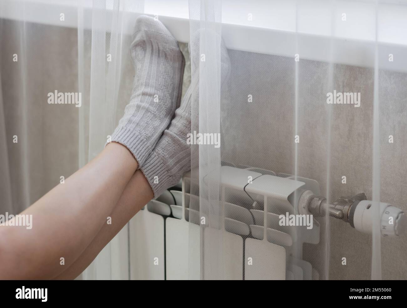 Woman warming up with feet on heater. Winter woolen socks drying on a ...