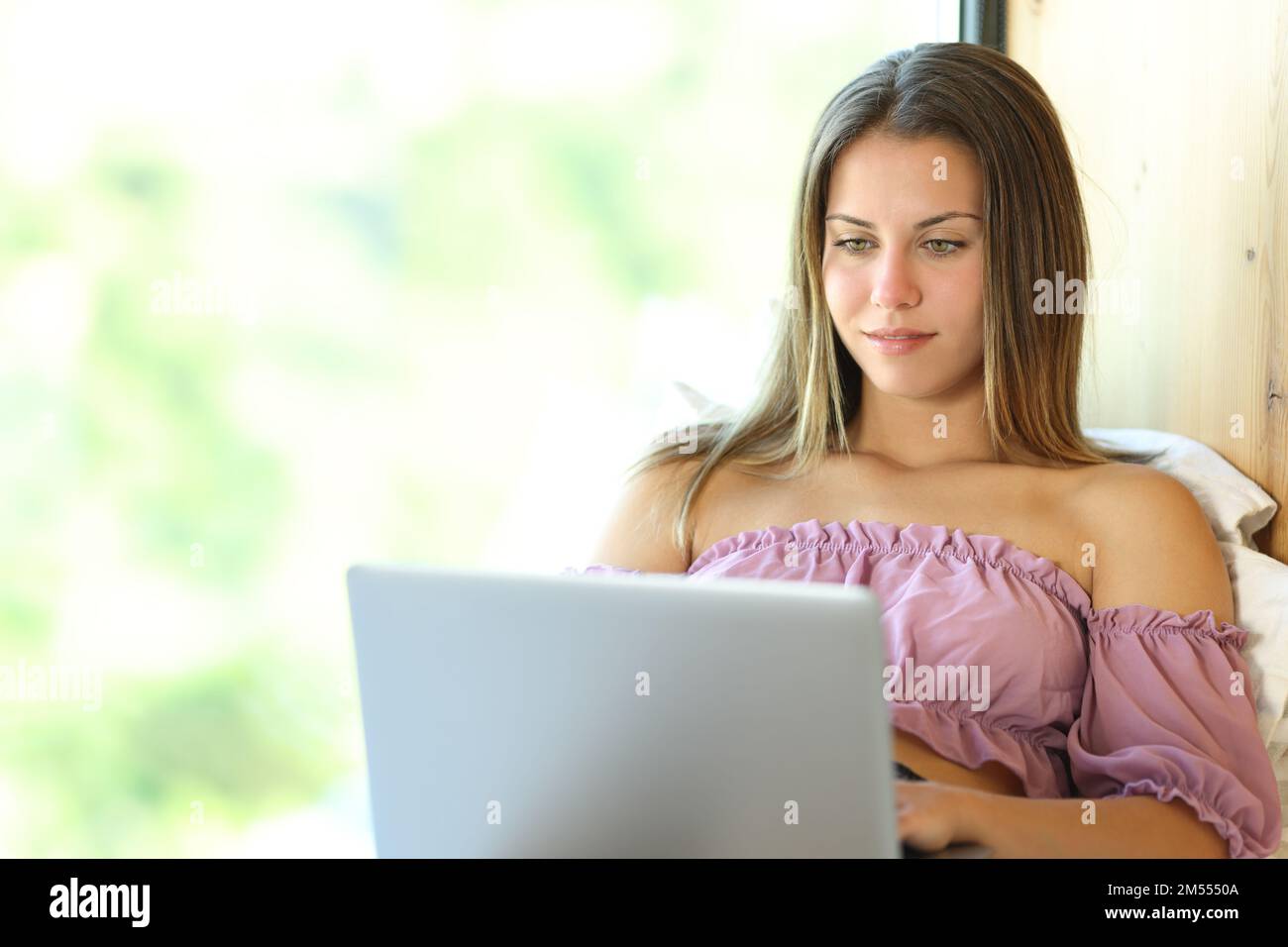 Teen using laptop near a window at home or hotel Stock Photo - Alamy
