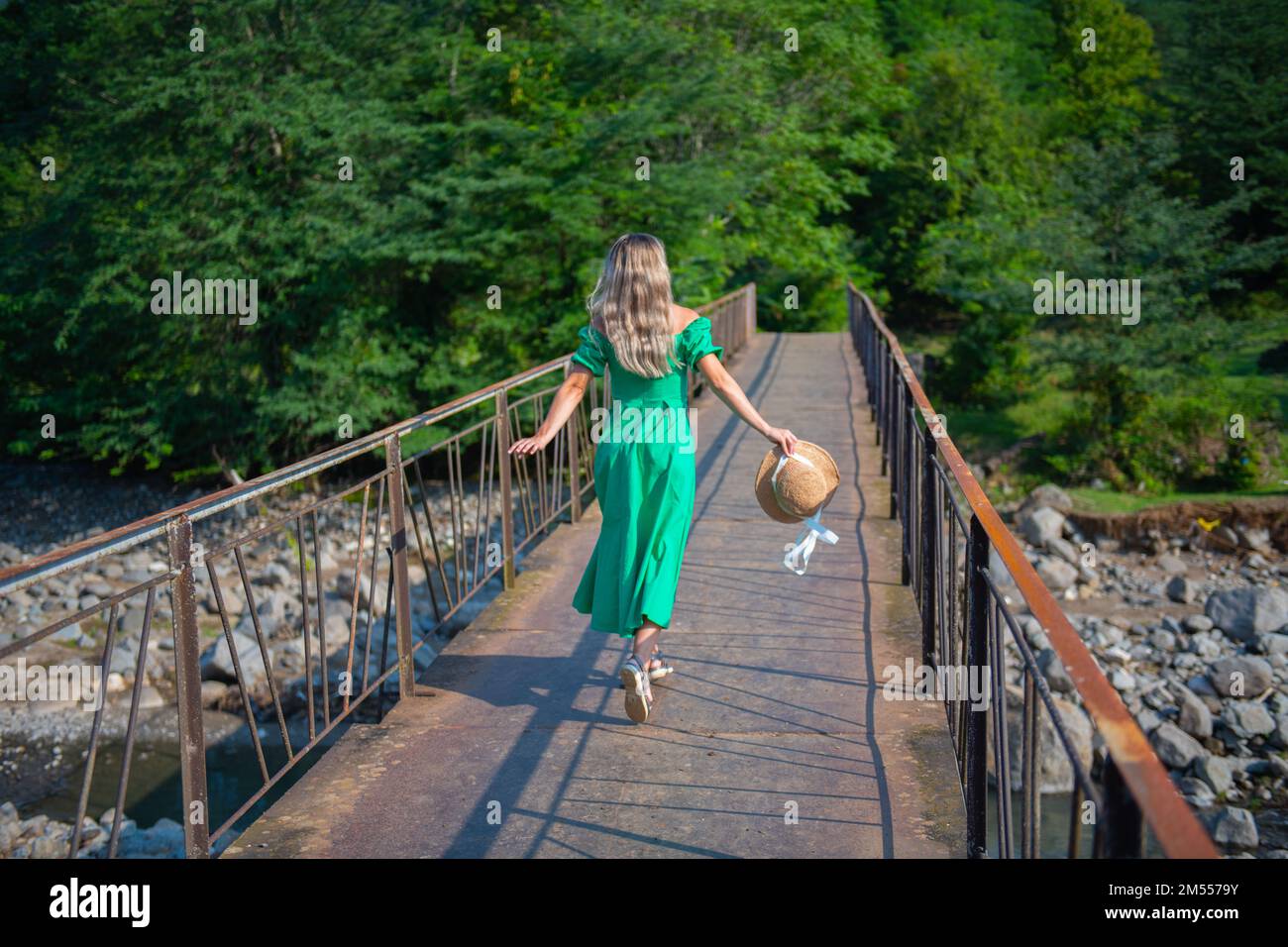 walks across the bridge deck in a green dress and hat in hand Stock ...