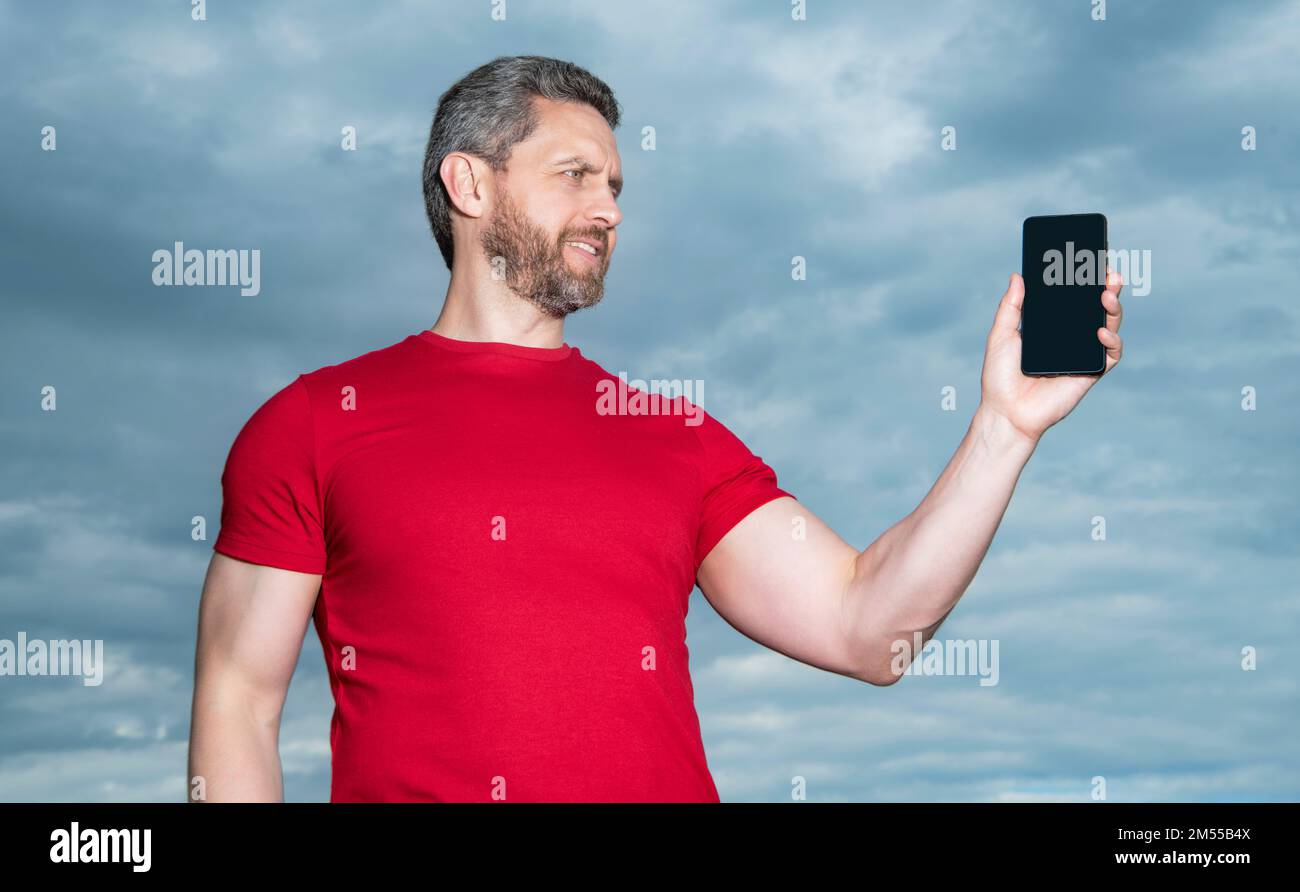photo of smiling man showing phone app. man showing phone app on sky ...