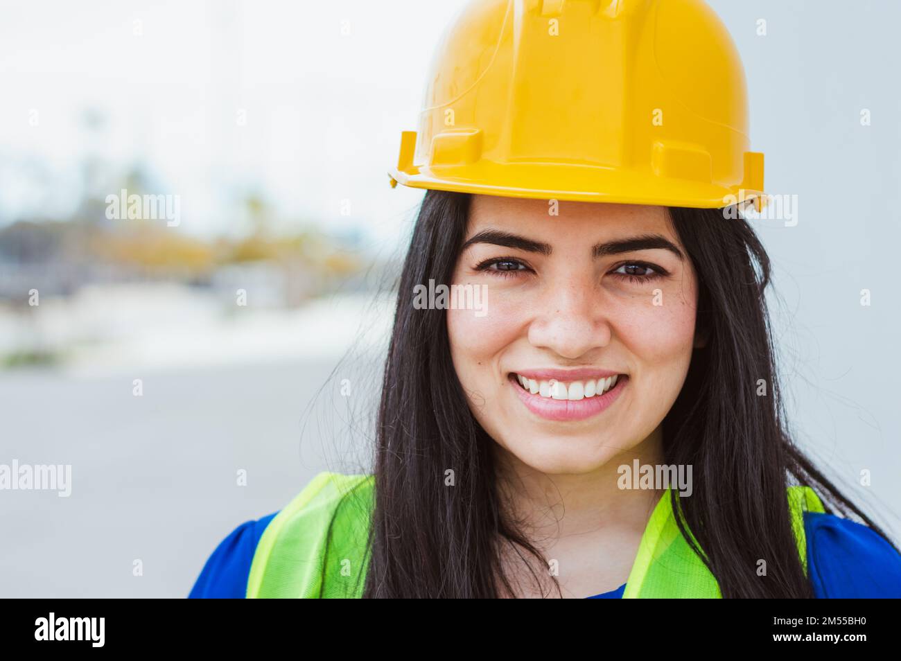young latin woman engineer, wearing safety helmet and vest, worker of a construction site ...