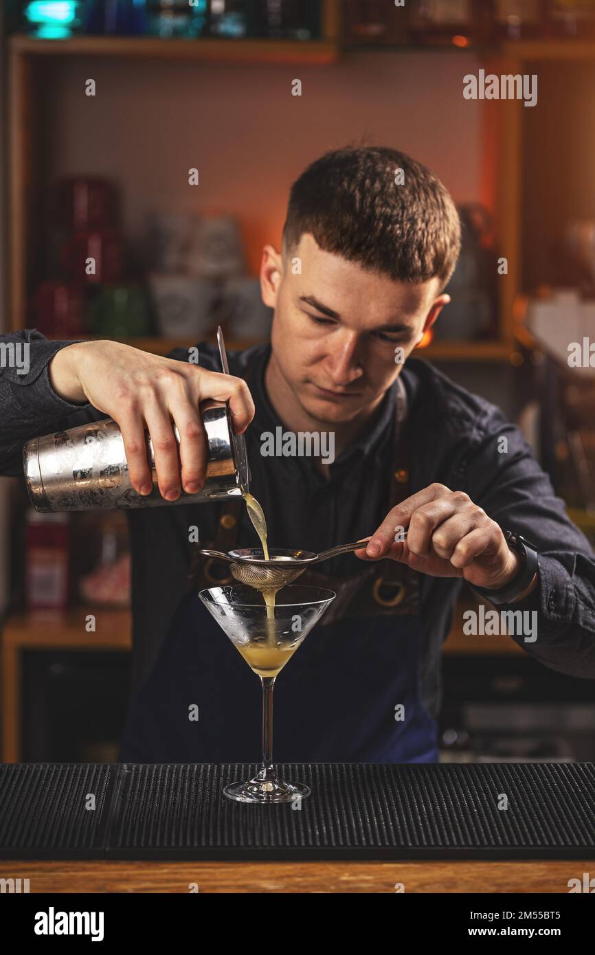Barman making a cocktail, pouring it into martini glass Stock Photo - Alamy