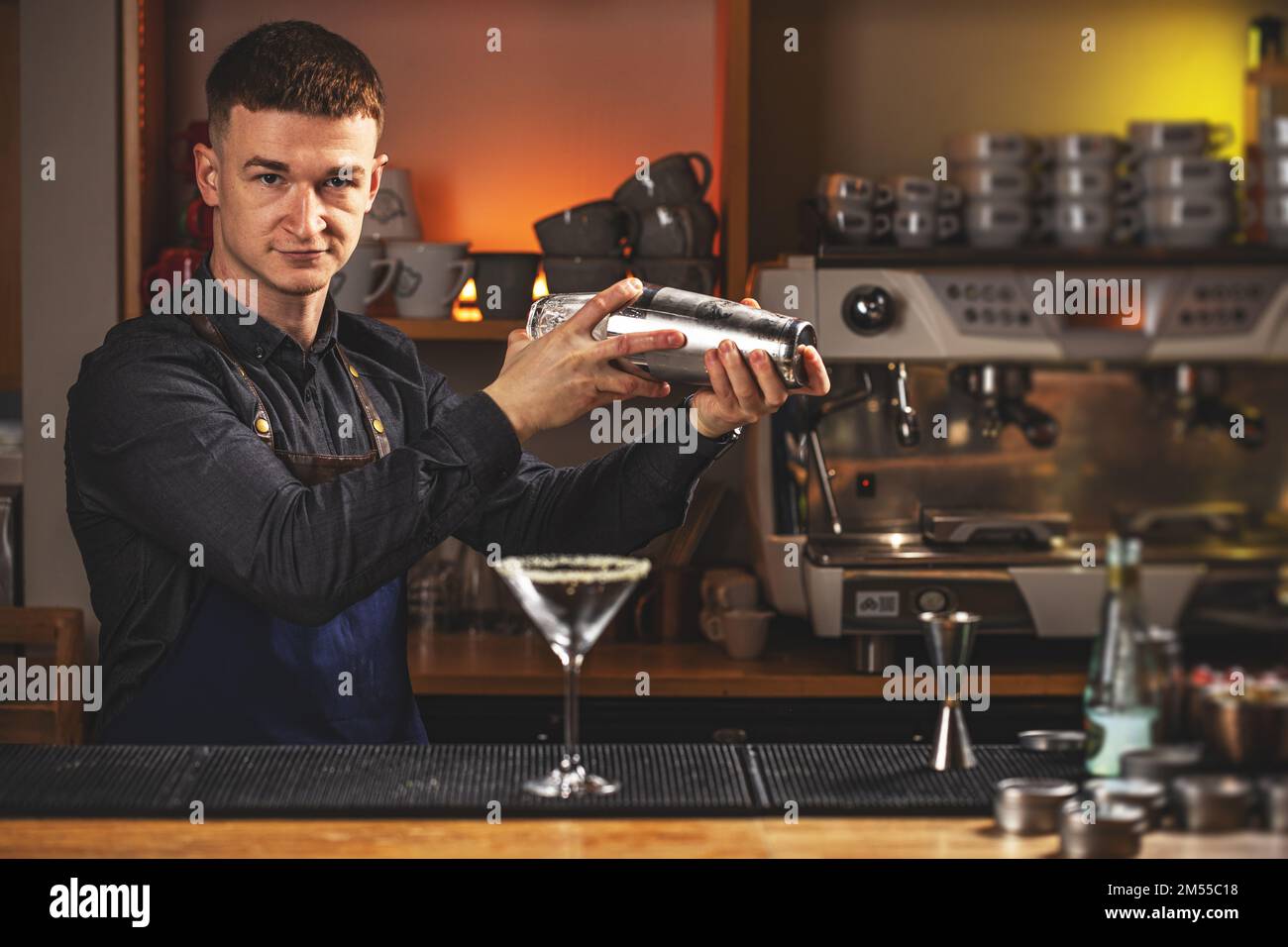 Professional bartender holds in hands steel shaker and mixing a ...