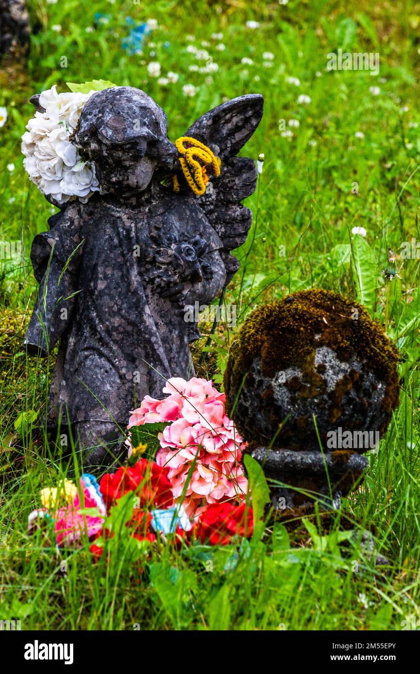 An old statue of a baby angel with colorful flowers around it in a ...