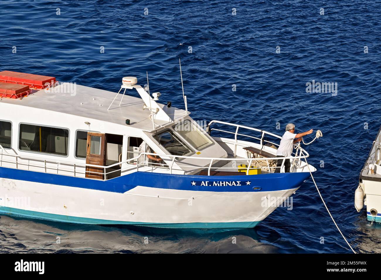 Patmos, Greece - May 2022: Crew member of a small motorboat throwing a ...