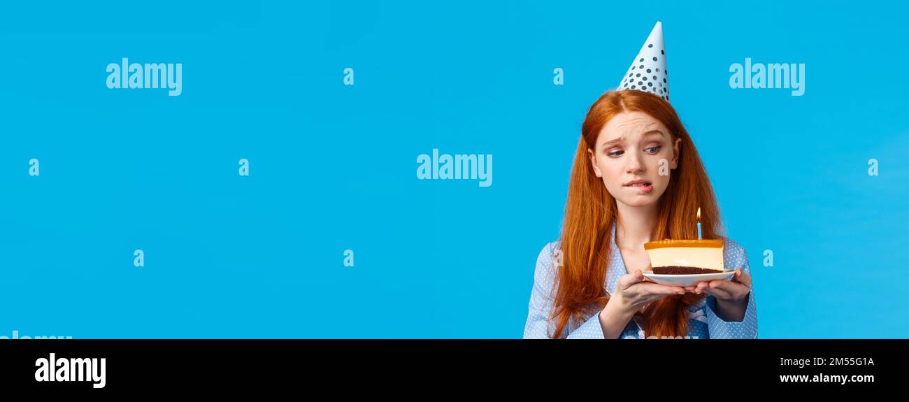 Attractive caucasian redhead woman in birthday cap, holding delicious ...